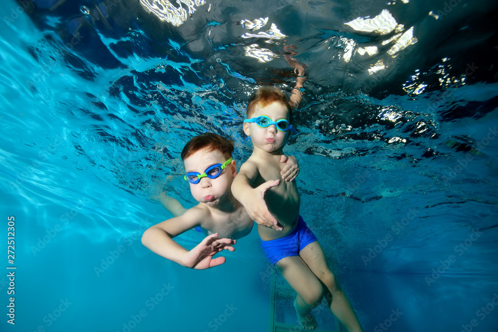 Two beautiful sports little boys swim, frolic, dance under the surface ...