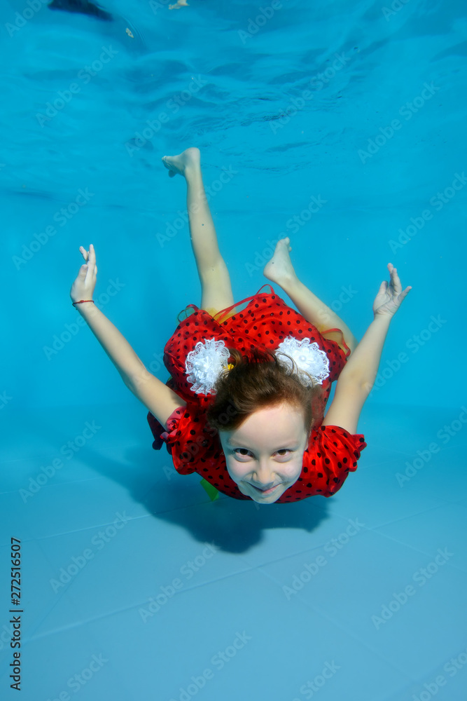 A little girl diving to the bottom of the pool in a red dress, with ...