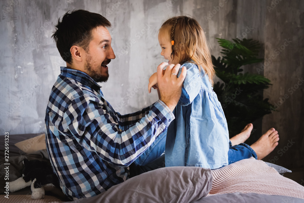 Dad and his daughter play on the bed in the bedroom, smiling and ...