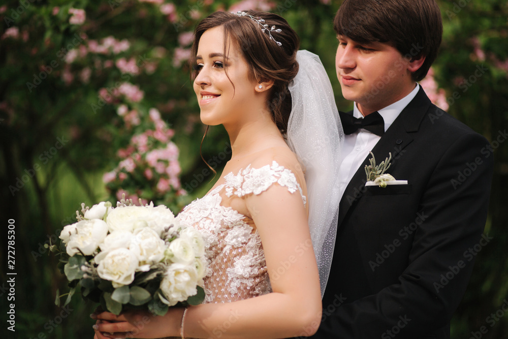 Handsome groom hug his beautiful bride. Newlyweds walking in the park ...