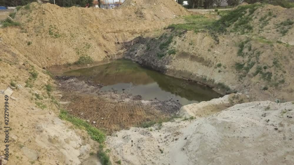 Ditch with water at the construction site with heaps of sand and earth ...