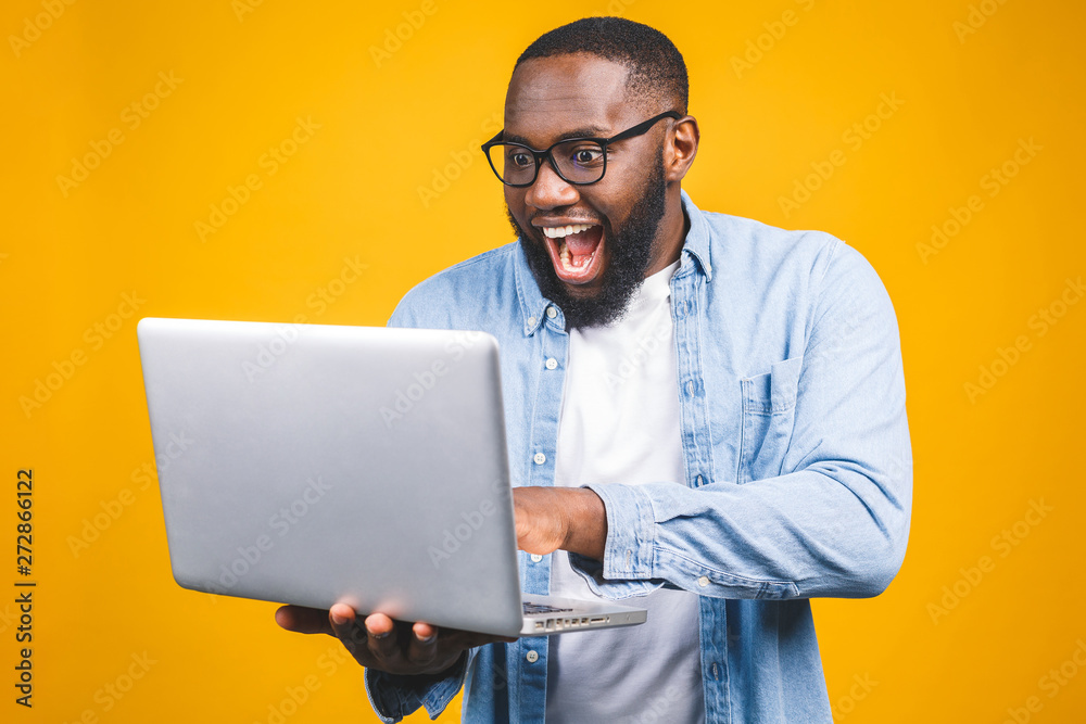 Young surprised african american man standing and using laptop computer ...