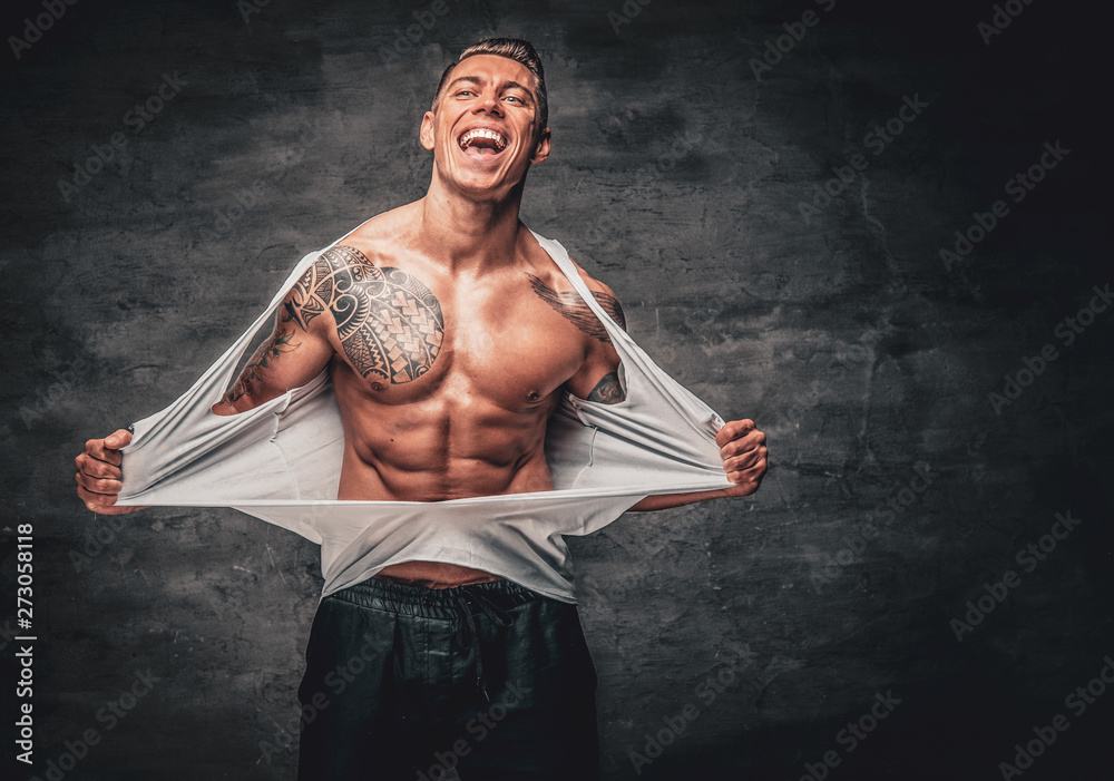 Studio portrait of athletic male with tattoo ripping t shirt on his ...
