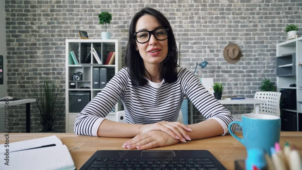 Portrait of cute young woman skyping in office talking waving hand ...