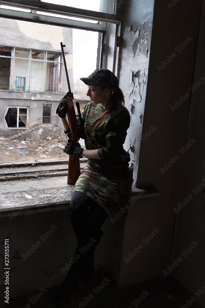 A young woman with a rifle in uniform at the window looking at the ...