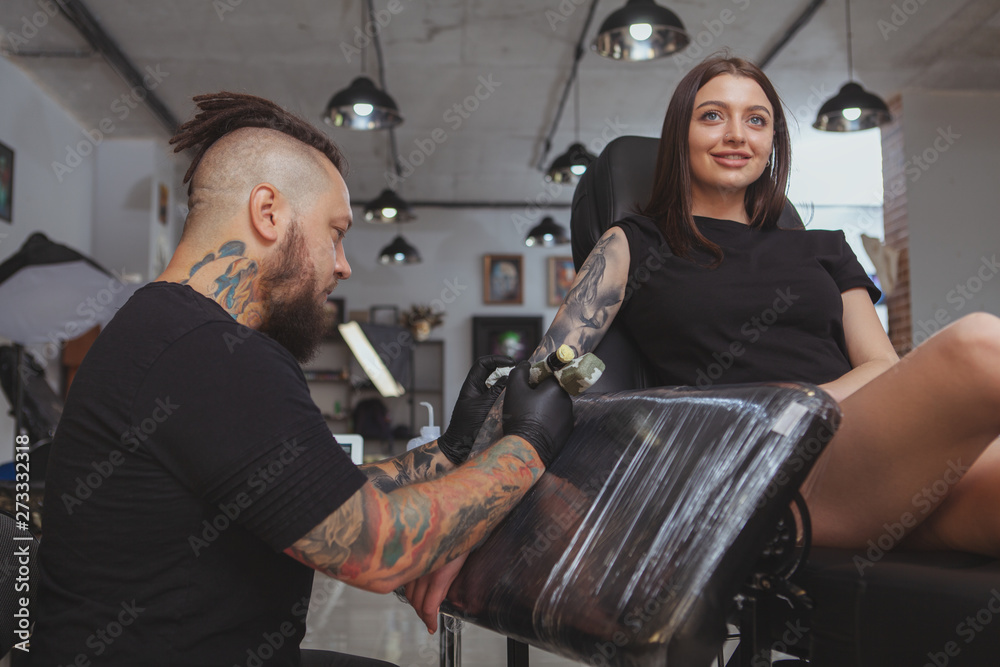 Low angle shot of a beautiful young woman getting arm sleeve tattoo by ...