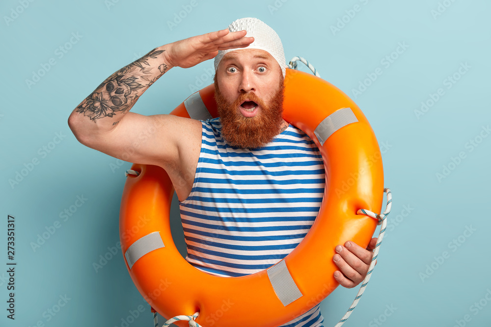 Shocked bearded red haired man looks surprisingly into distance, keeps ...