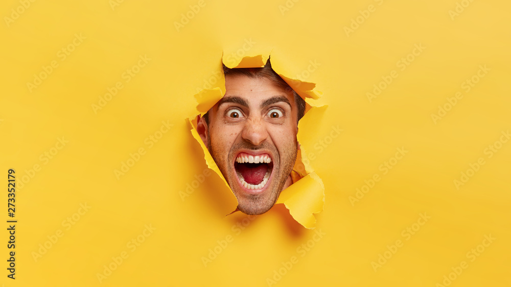 Angry male face through yellow paper hole. Outraged man sticks head ...