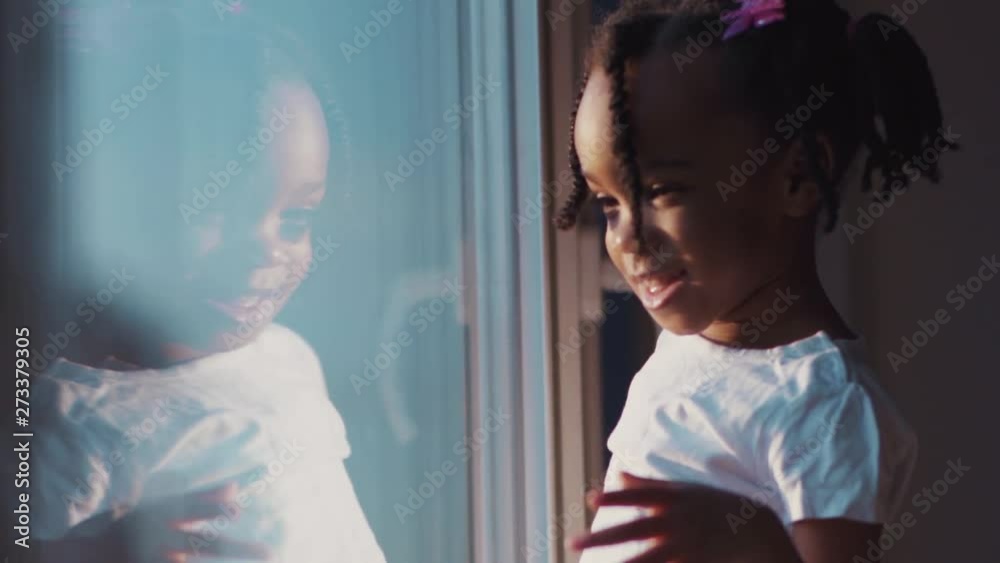 Curious afro-american little girl touching the window looking at lovely ...