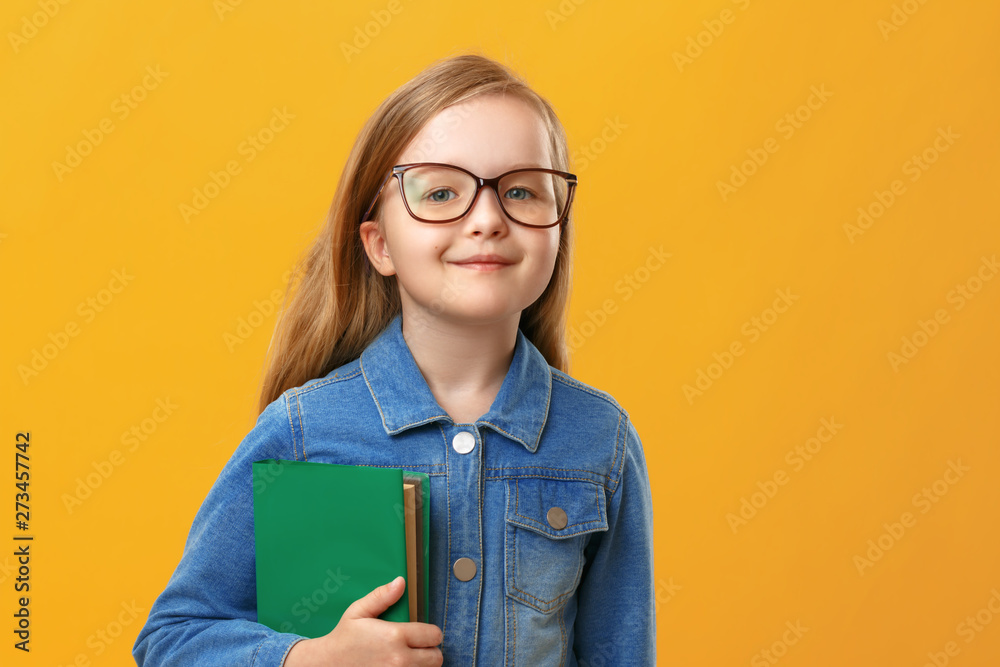 Little student girl in denim shirt on a yellow background. A child with ...