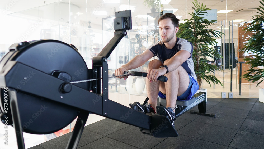 Fitness serious young man using rowing machine in the gym.Exercises to ...