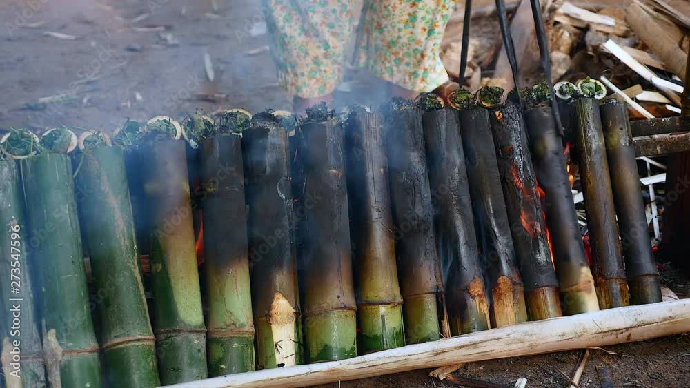 Woman turning bamboo cakes cooking on fire; Bamboo cakes are made of ...