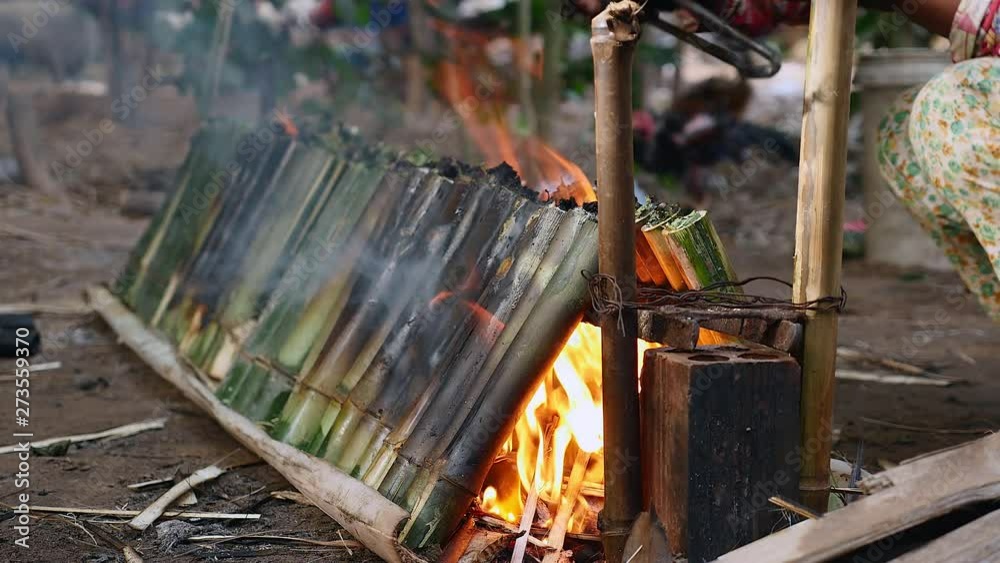 Woman turning bamboo cakes cooking on fire; Bamboo cakes are made of ...