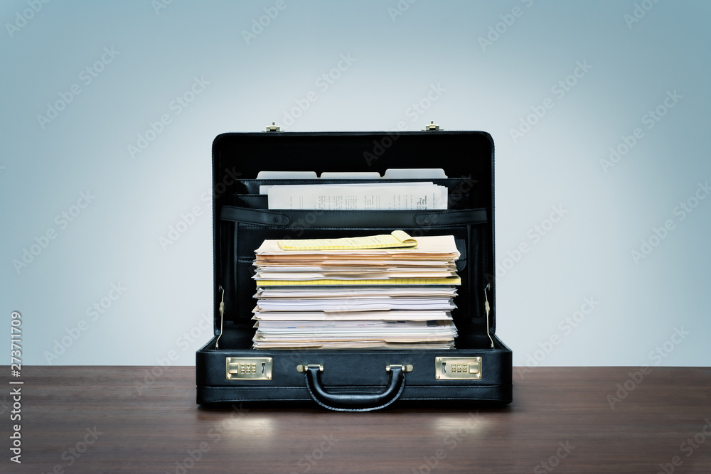 Tall stack of files and folders in black leather briefcase on wood desk ...