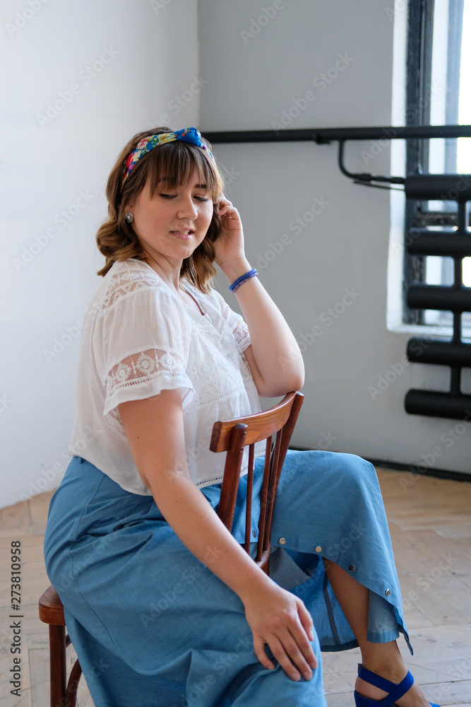 A young plus size woman sits on a chair in a spacious white room. Smile ...