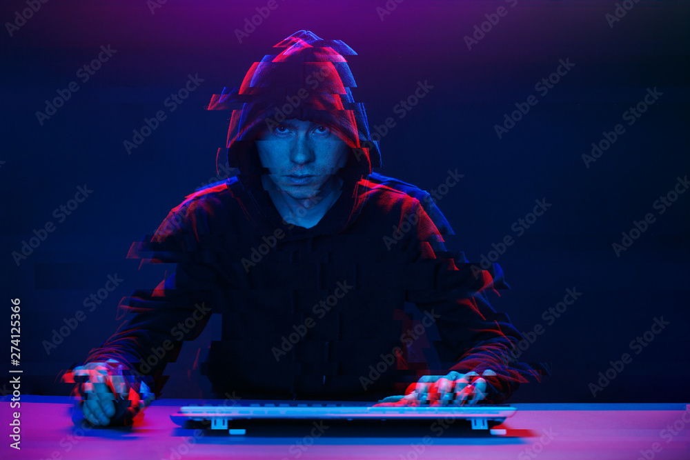 Hacker in the hood working with computer typing text in dark room. Image with glitch effect ...