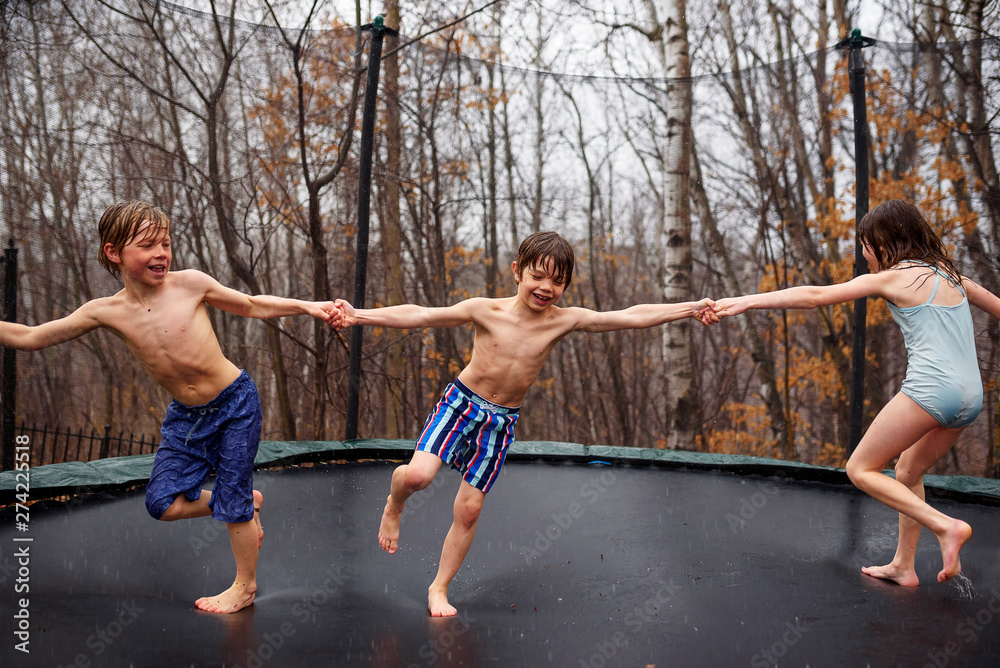 Three children jumping on a trampoline in the rain Stock Photo | Adobe ...