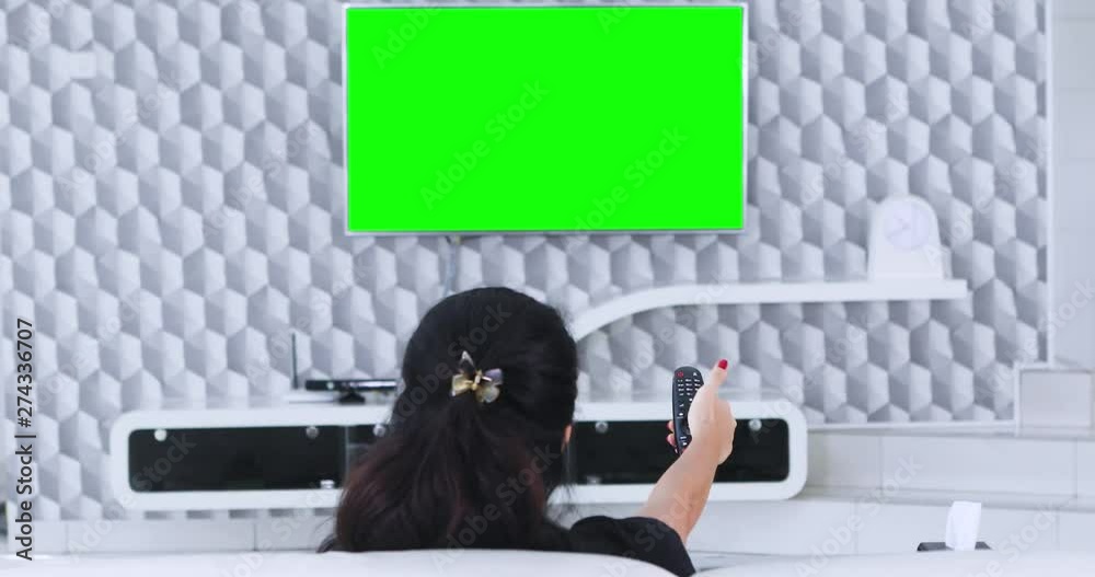 Back view of young woman watching TV with green screen in the living ...