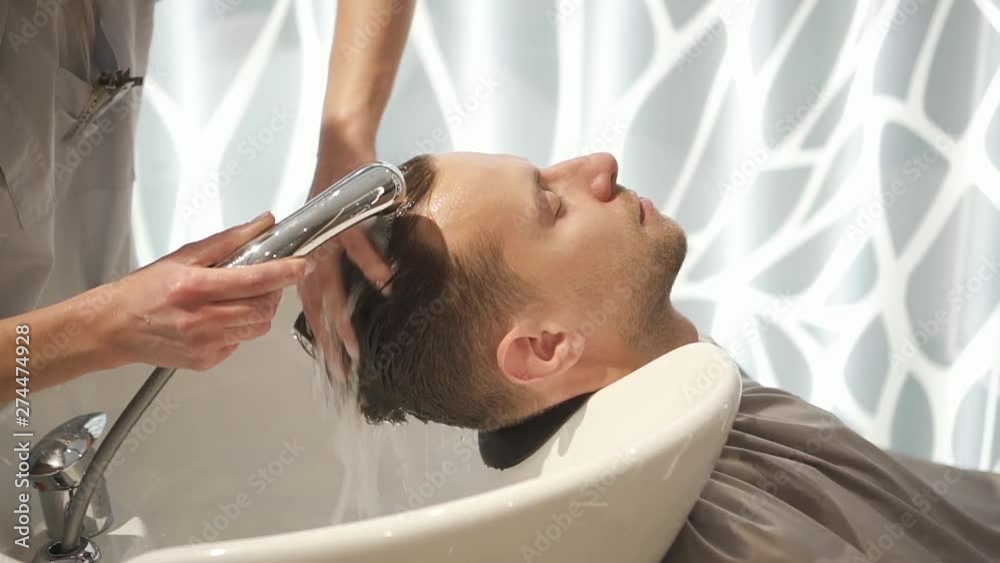 Professional woman is carefully washing and cleaning young man head ...