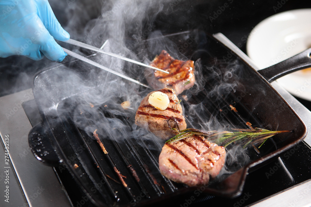 Cooking a piece of beef on the grill indoors. Cooks hands in the frame ...