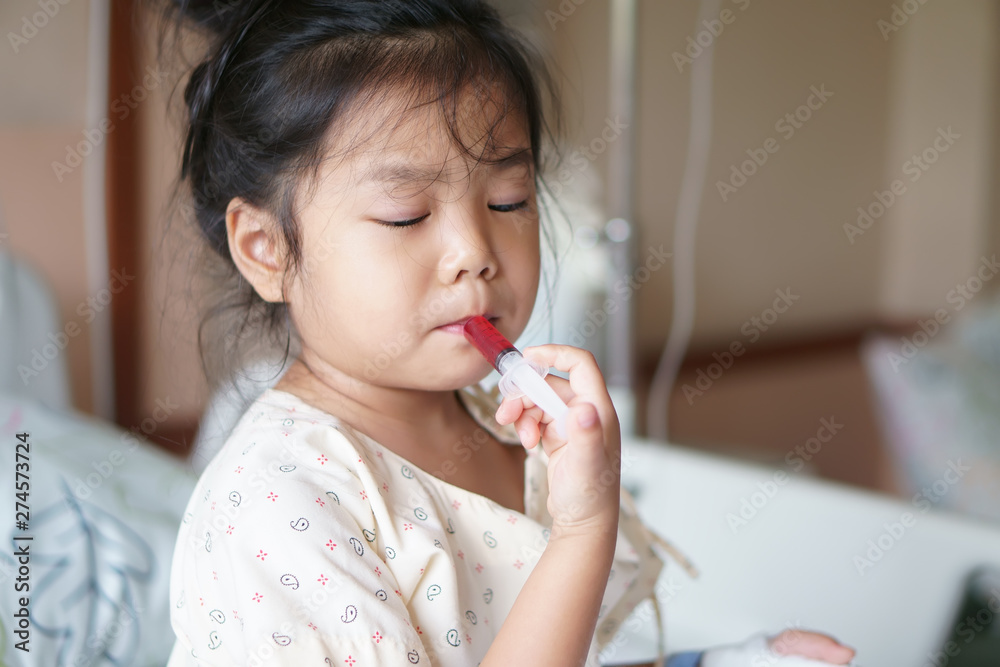 Asian child cute or kid girl Influenza sick holding and eating or taking sweet red drug or water ...