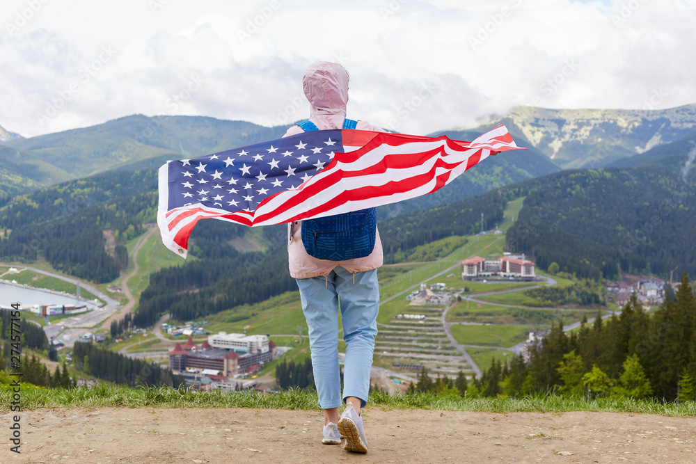 Fotka „Back view of travel standing at top of hill holding USA flag on ...