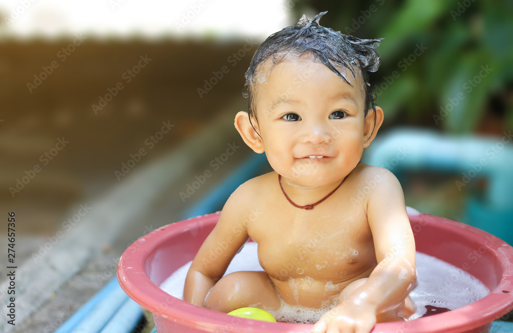 In the summer season, Asian baby child girl take a shower in a bathtub ...