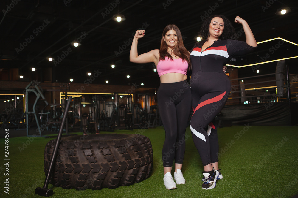 Two happy confident plus size women smiling, flexing their biceps at ...