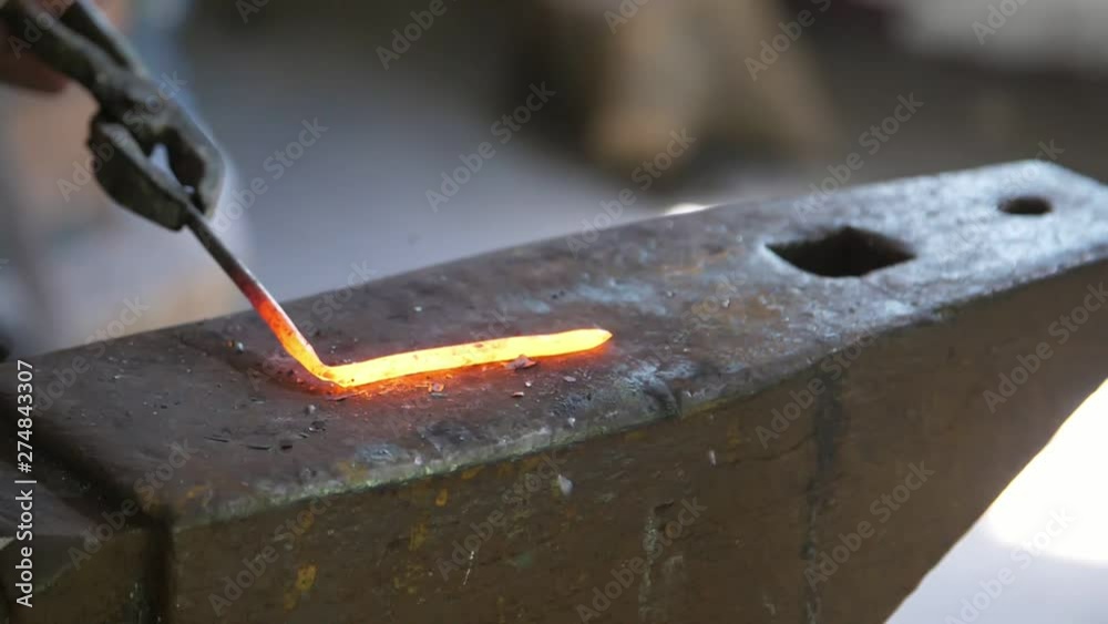 Blacksmith bending a metallic rod to make an iron rose in a dim smithy ...