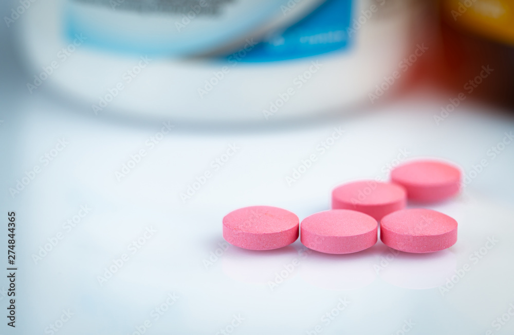 Round pink tablets pill on blurred drug bottle. Vitamins and minerals ...