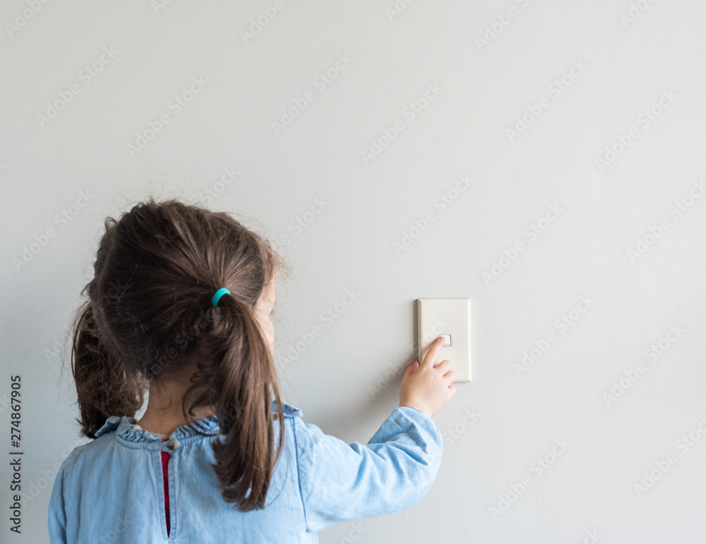 Rear view of little girl turning off Australian light switch on neutral ...