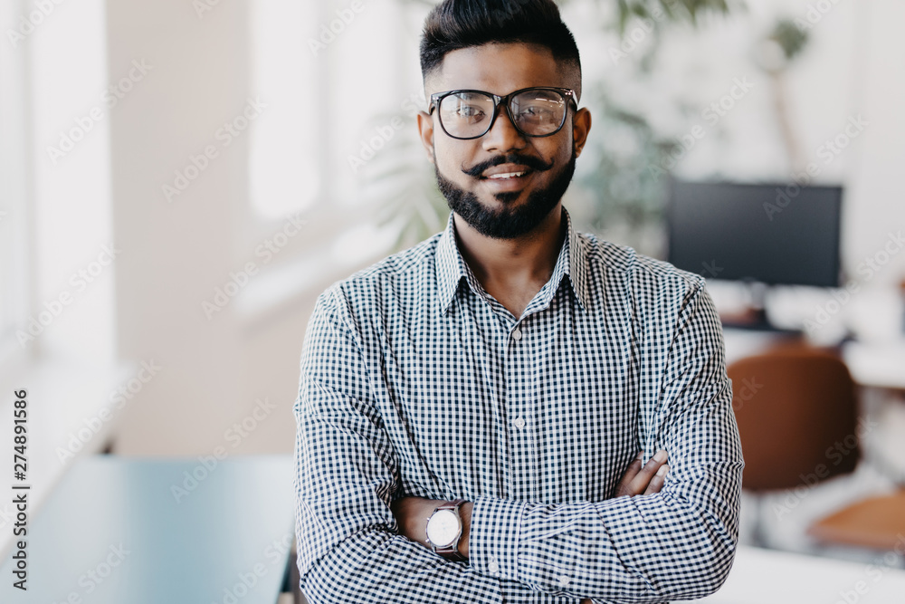 Portrait of smiling Indian man crossed arms standing at modern office ...