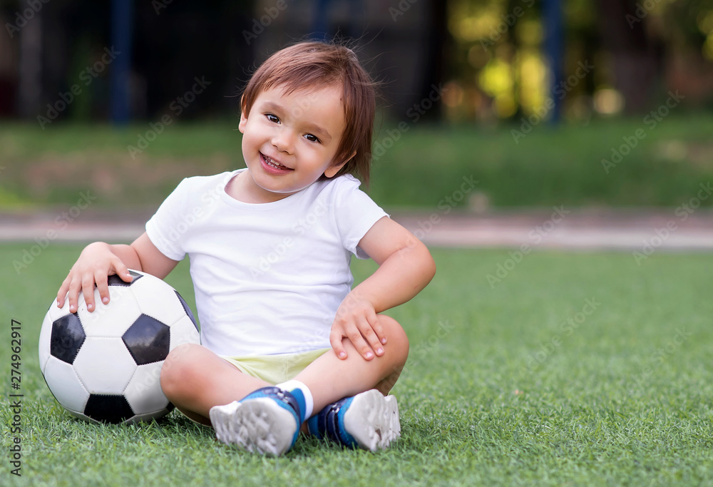Little toddler boy sitting with legs crossed on football field in ...