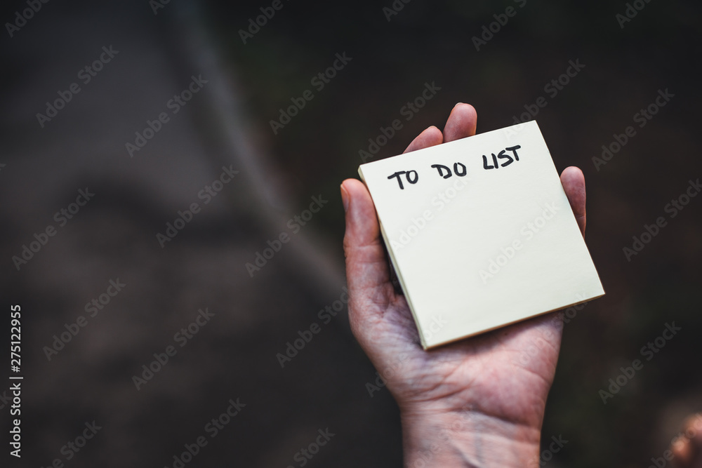 Young person’s hand holding yellow sticky note with the text to do list ...