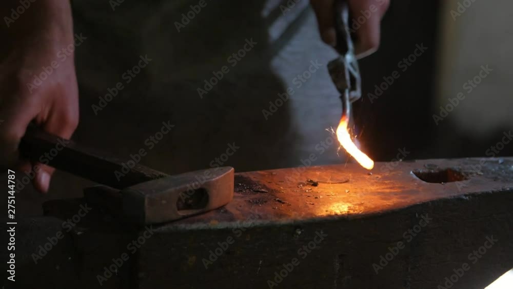 Blacksmith hitting a molten iron rose with a hammer on an anvil in an ...