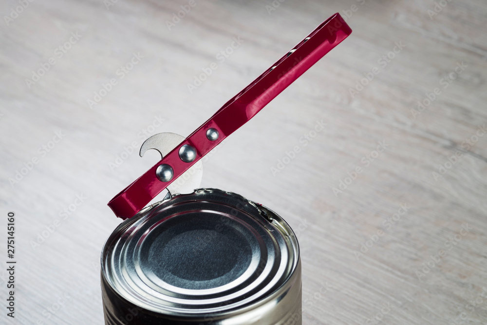 Opening a tin can with a can opener. The can opener is on the tin can ...
