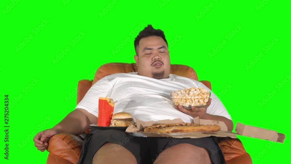 Overweight young man looks bored eating snack and junk foods. Shot in ...