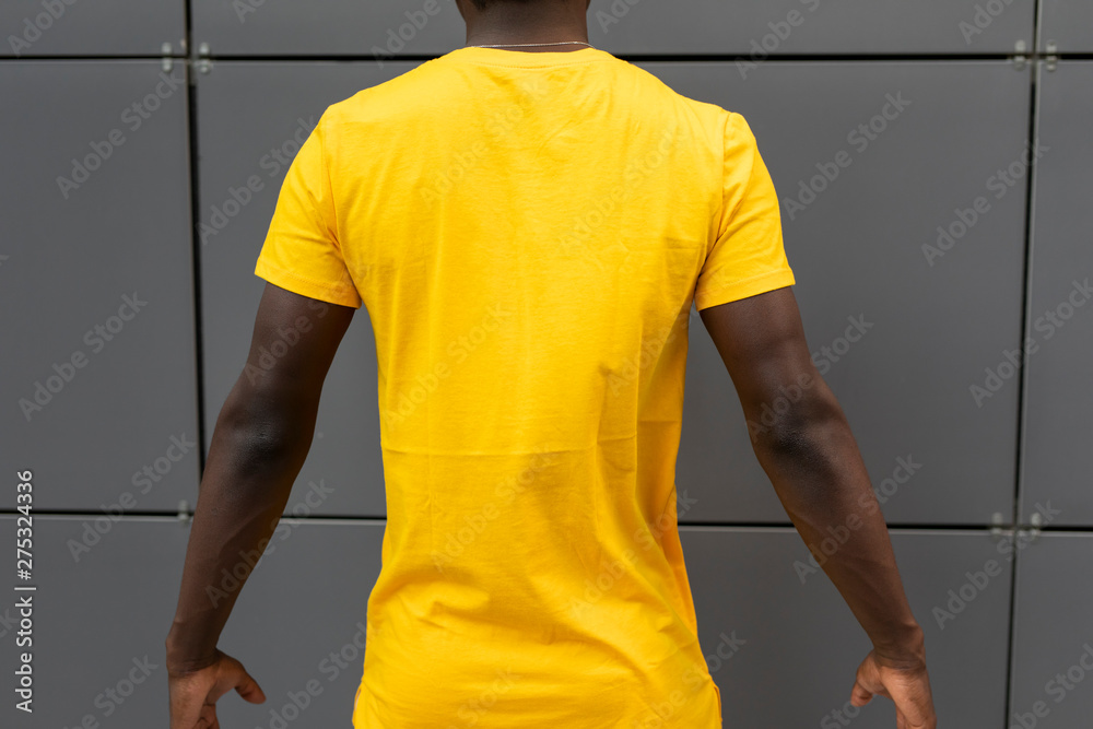Empty blank yellow t-shirt on the american male back standing near wall ...