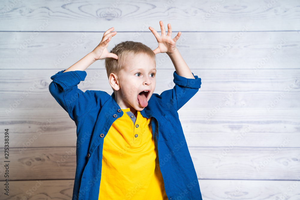 Little boy with his hands over the head shows his tongue in studio ...