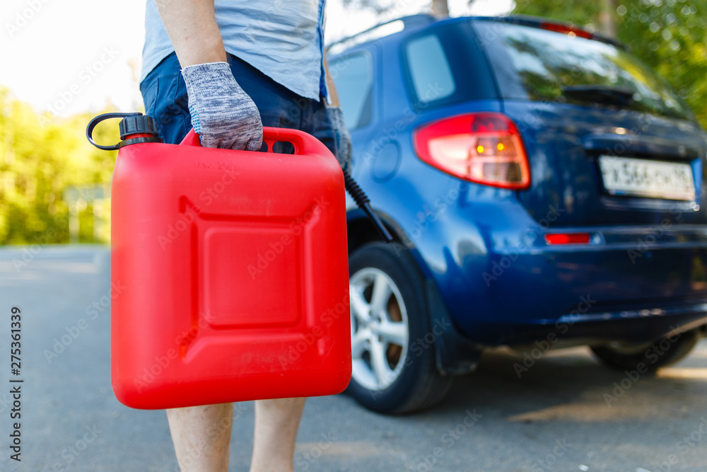 Man with a gas can on the side of the road with his car in background ...