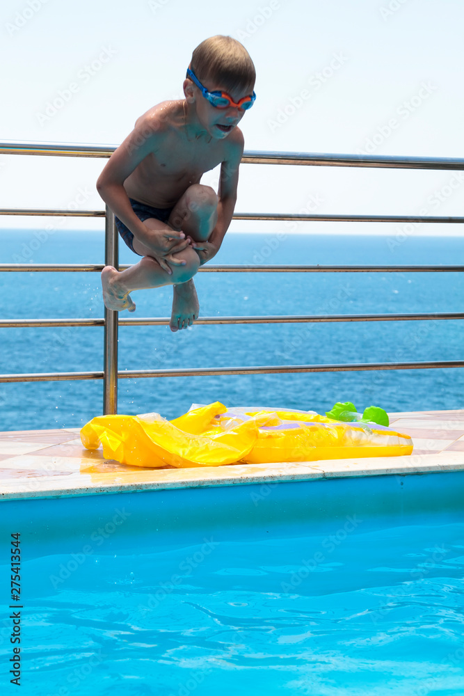 boy in a Villa on the sea jumps into the blue water of the pool with ...