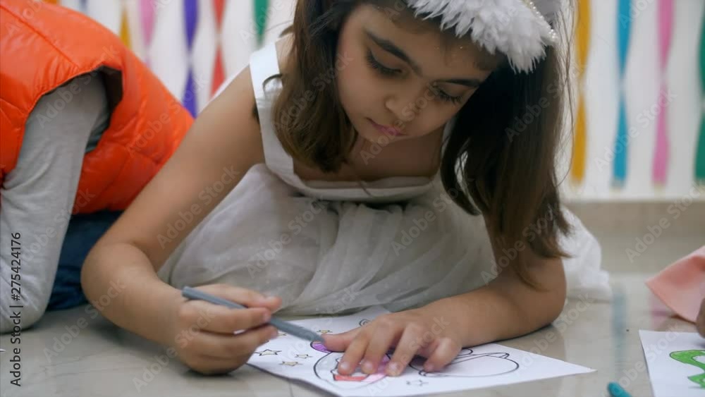 Calm and beautiful little girl coloring a sketch lying on the floor ...