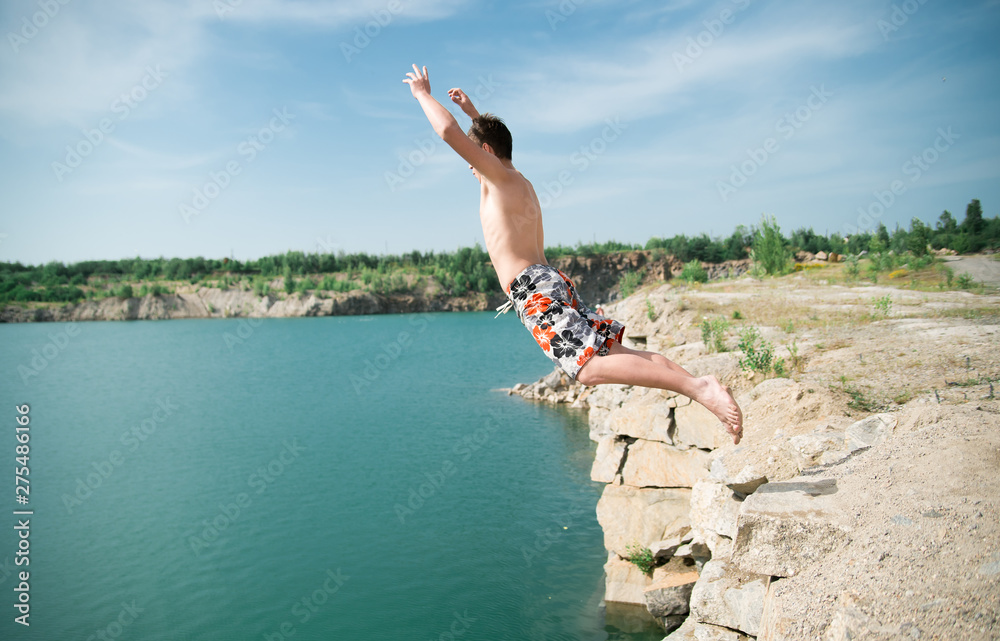 Young man jumping off cliff into blue water. Active outdoor, holiday adventure, healthy summer ...