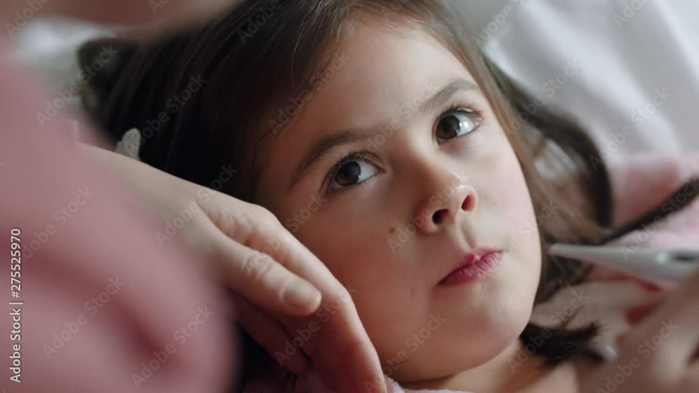 mother caring for sick child lying in bed with flu measuring temperature using thermometer ...