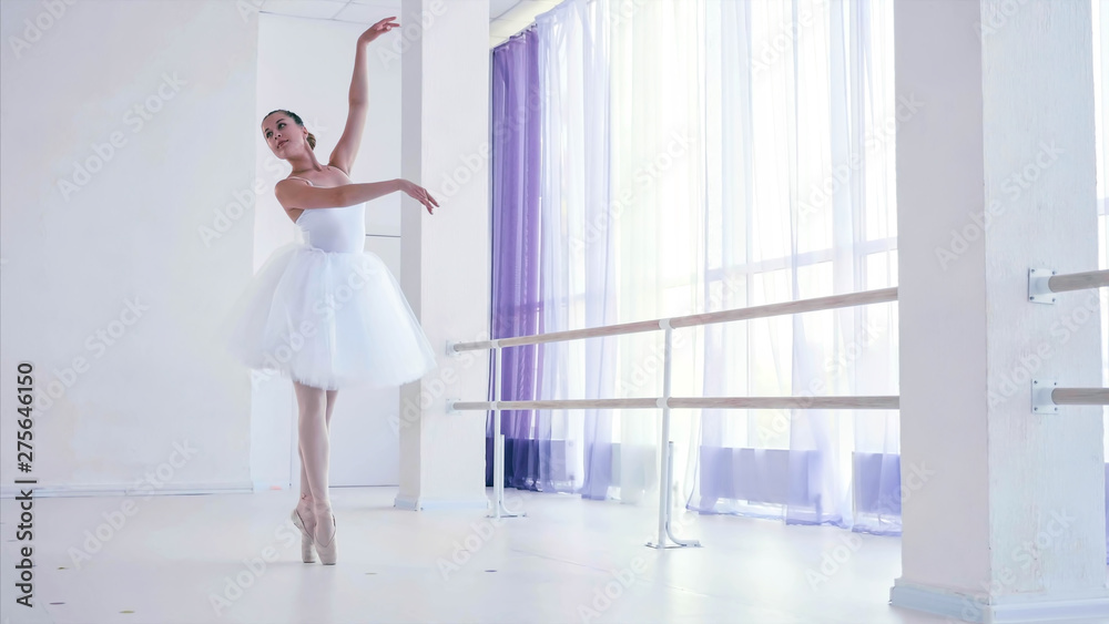 Ballet dancer in white tutu and pointes is dancing in ballet studio ...