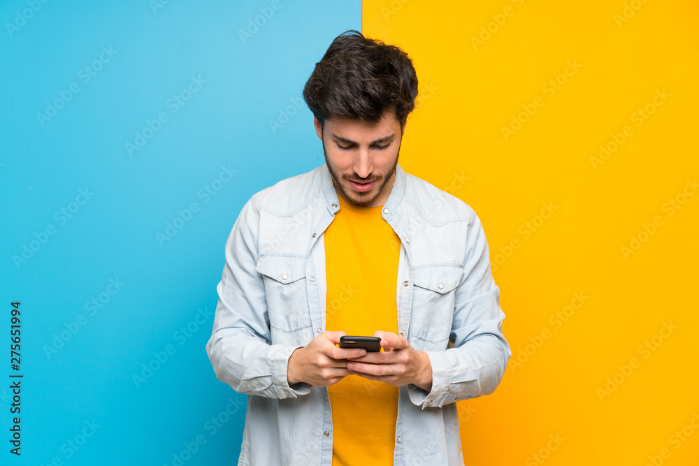 Handsome over isolated colorful background sending a message with the ...