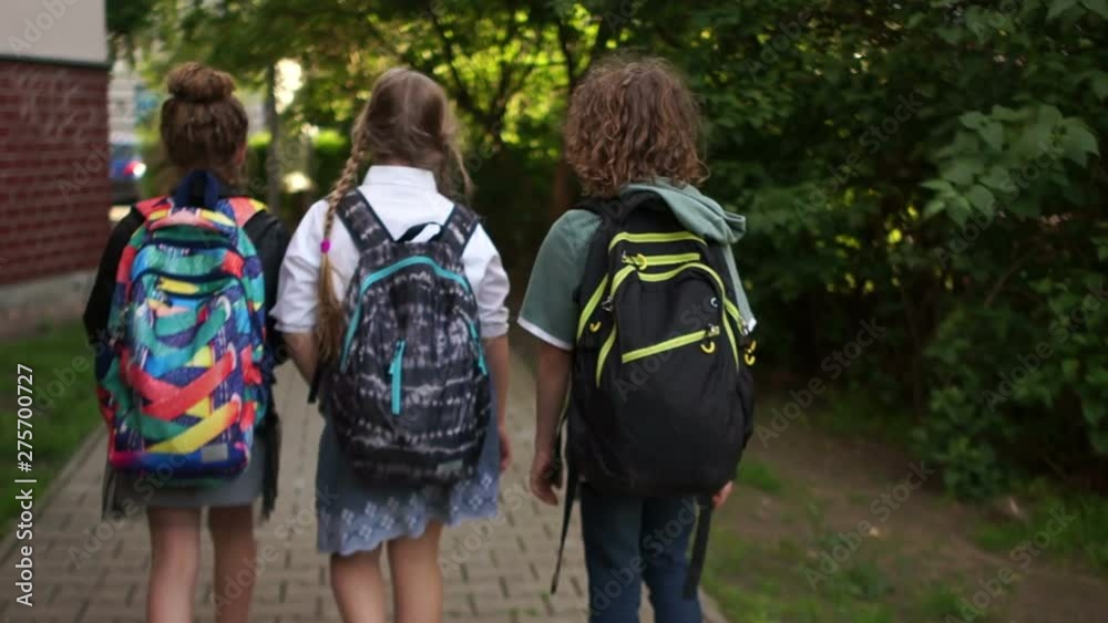 Three teen school students go to school on city streets past cars. Back ...