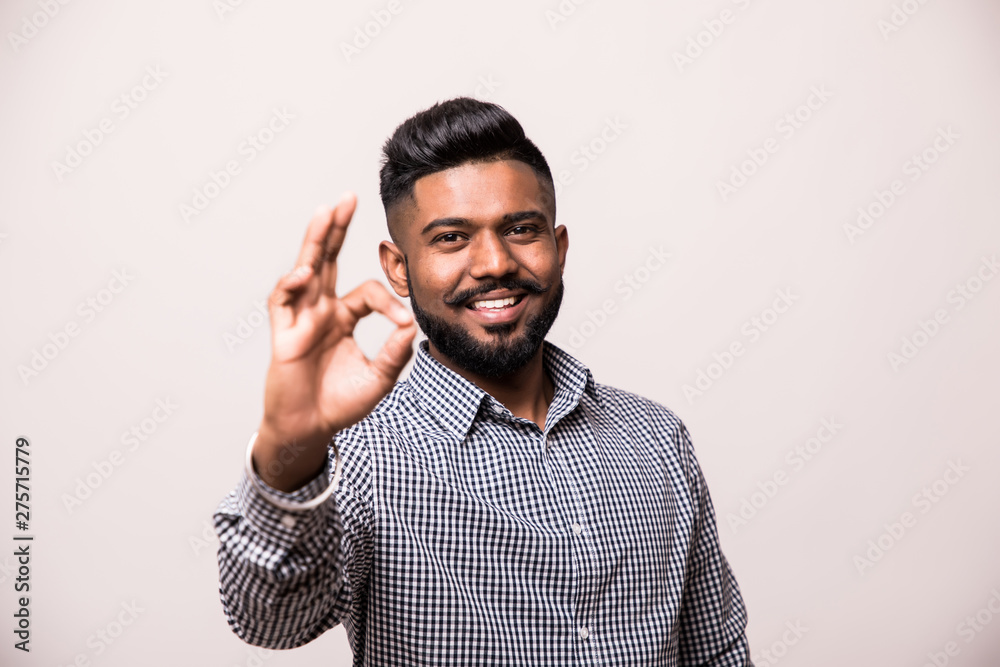 Young indian man over isolated white wall showing ok sign with fingers ...