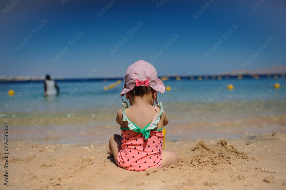 back view photo of a little girl in swimsuit and pink hat sitting on ...