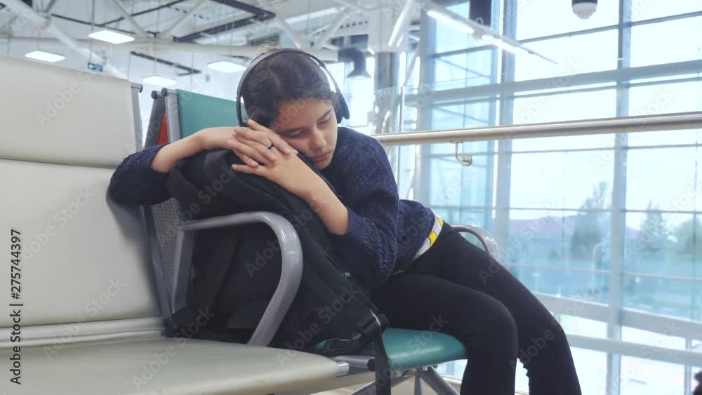 Tired girl teen in headphones traveler sleeping on the airport waiting for the plane departure ...